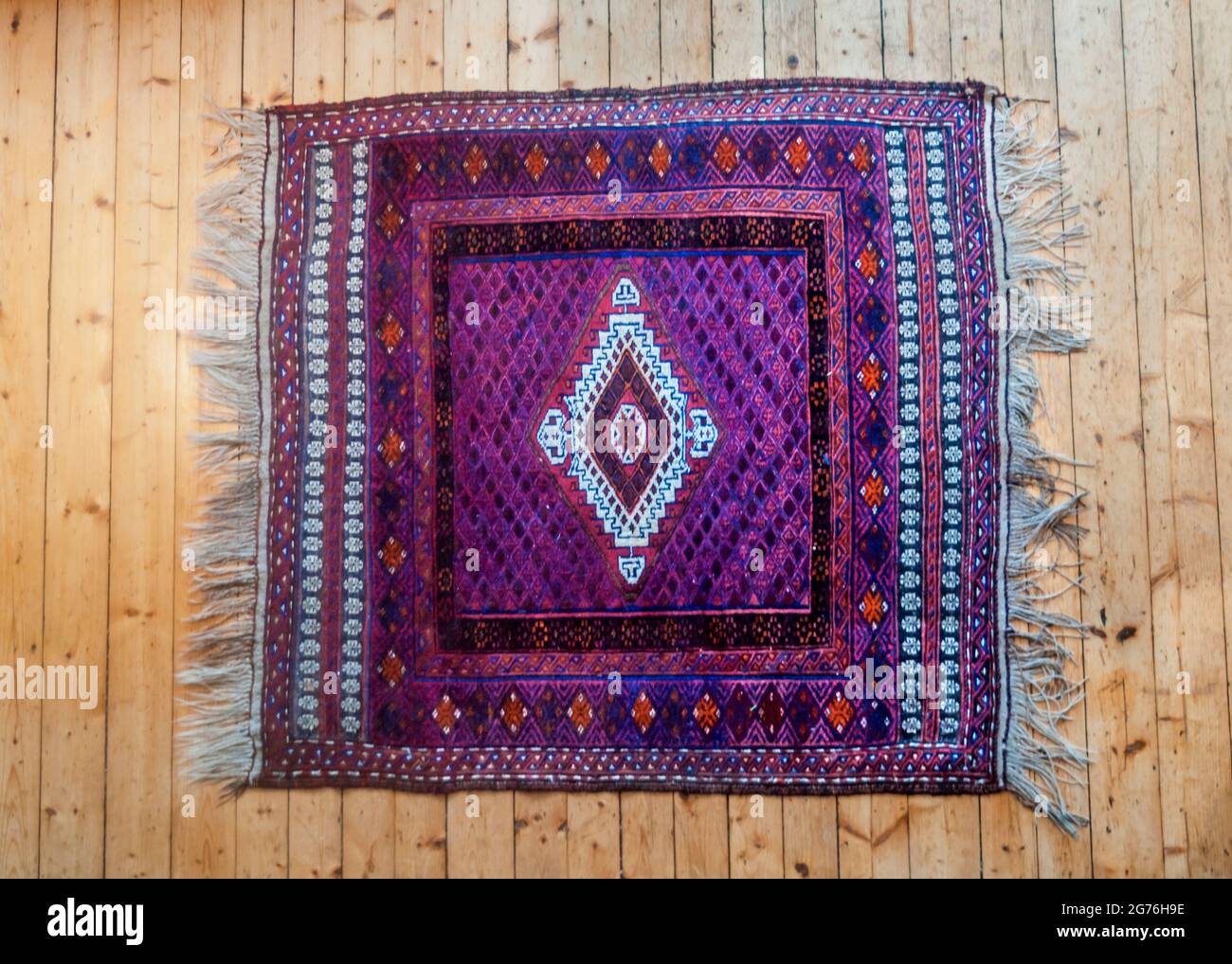 A handmade tribal rug from Afghanistan on a floor with knotty pine ...