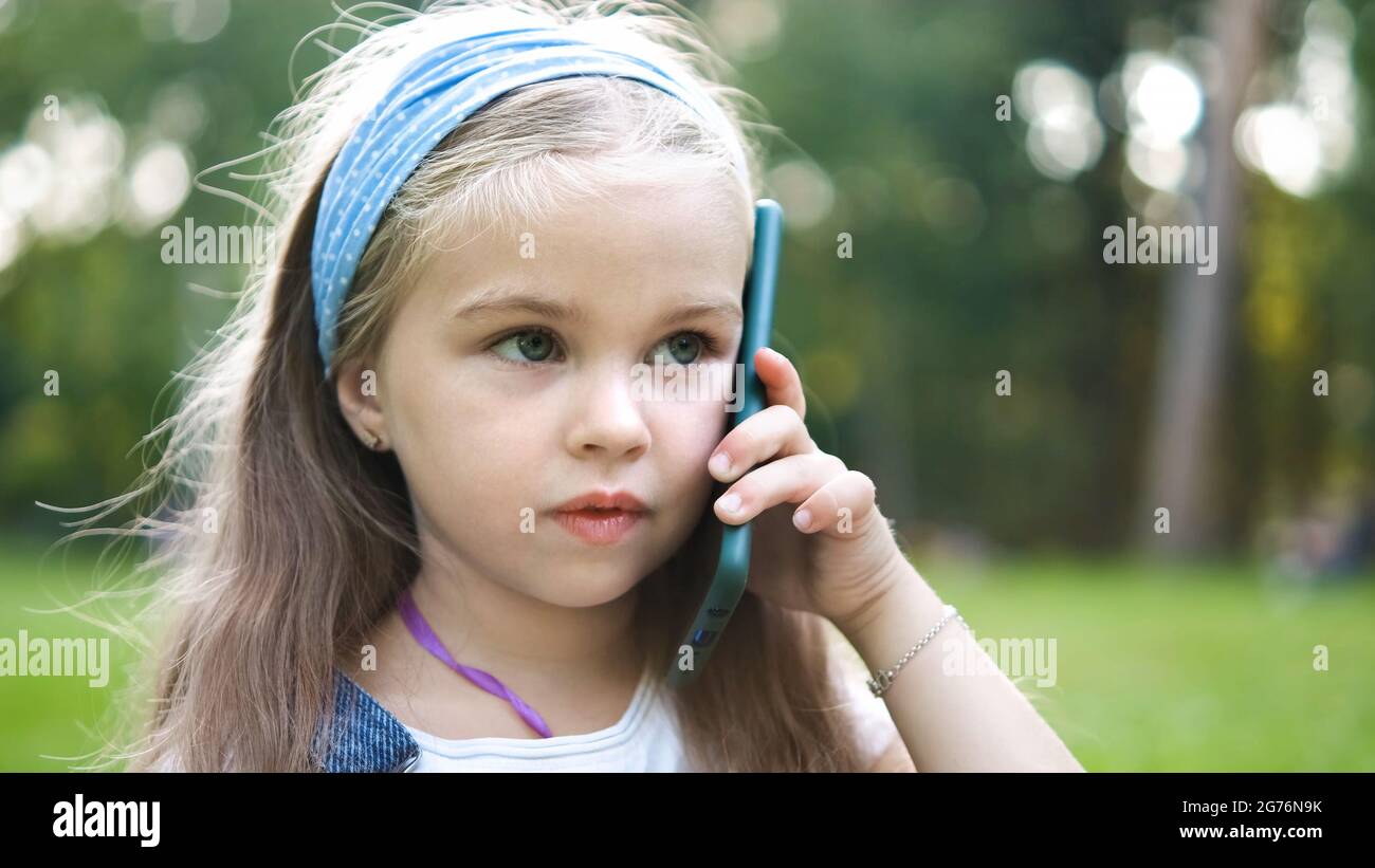Positive little child girl having conversation on her mobile phone in ...