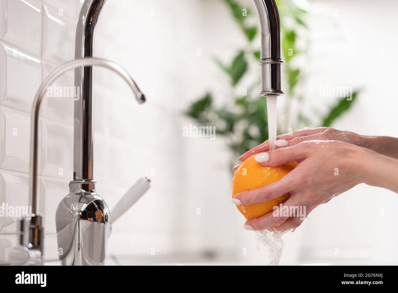 Female washing orange fruit in fresh water from kitchen sink crane ...