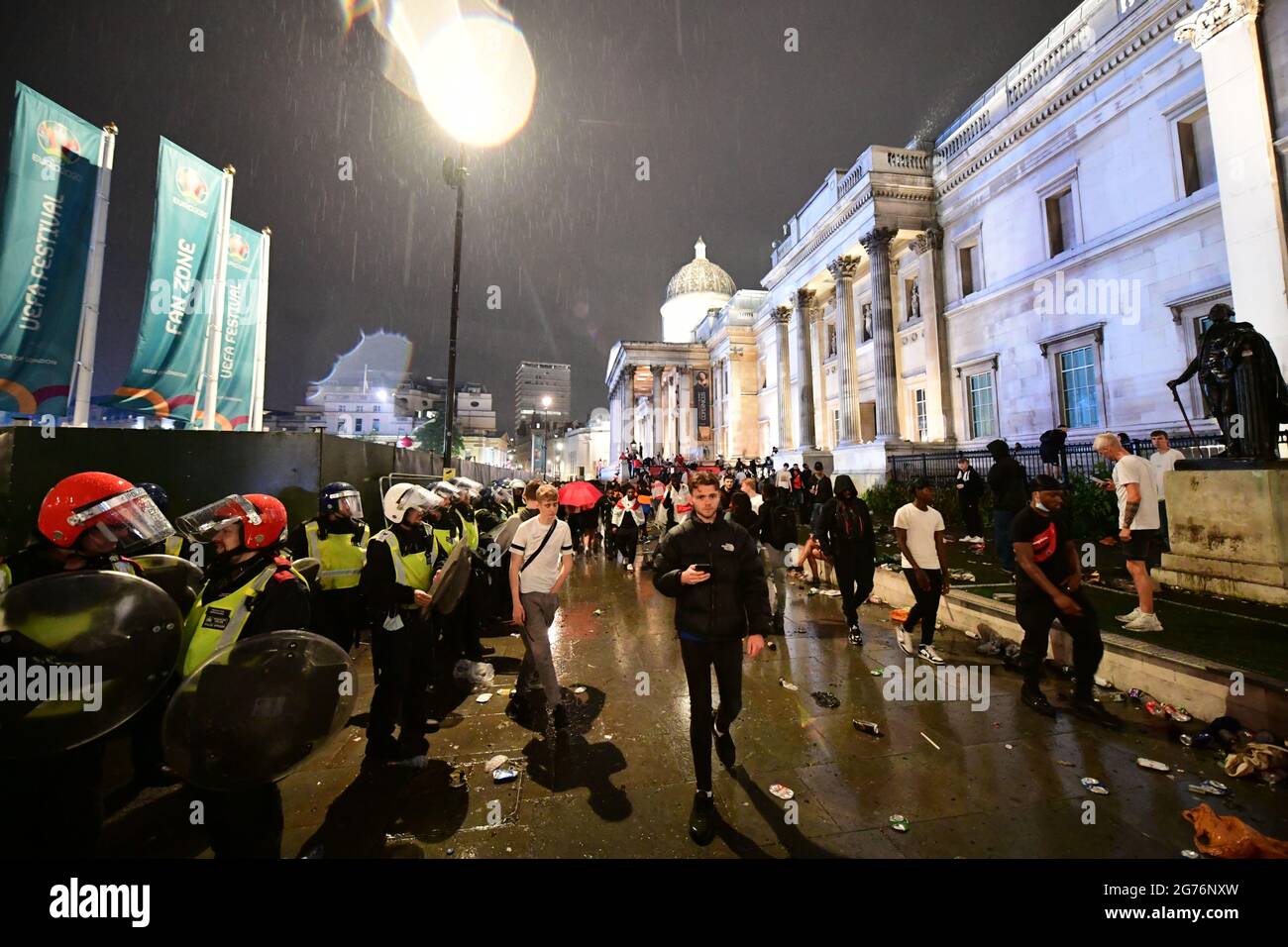 Dejected England fans walk past police officers in riot gear as they ...