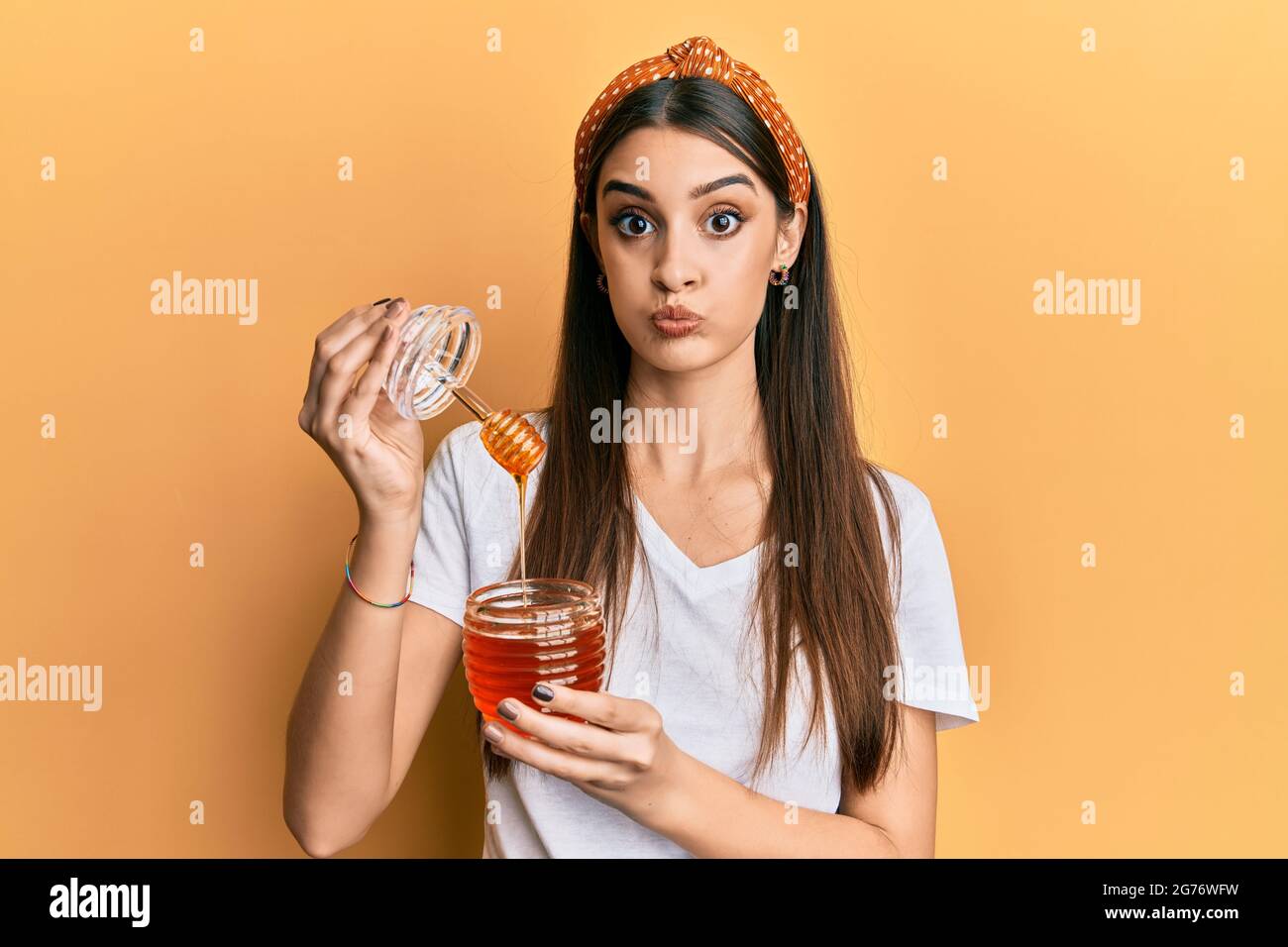 Beautiful brunette young woman holding honey puffing cheeks with funny ...