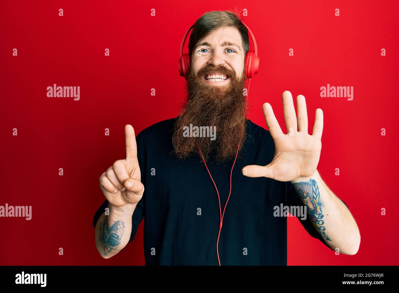 Redhead man with long beard listening to music using headphones showing ...