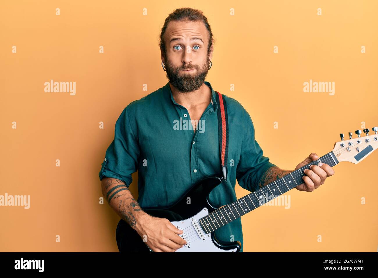 Handsome man with beard and long hair playing electric guitar puffing ...