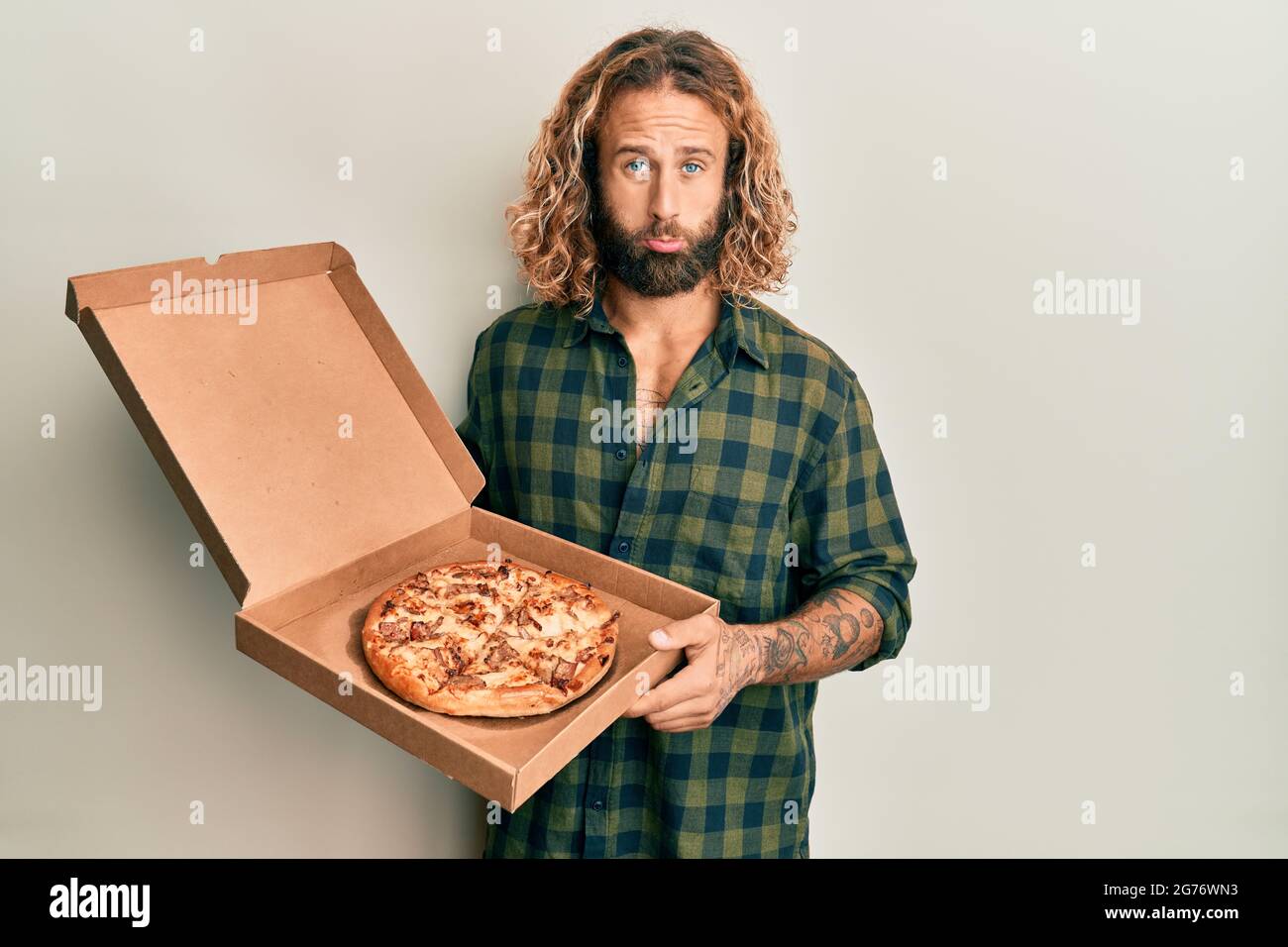 Handsome man with beard and long hair holding italian pizza depressed ...
