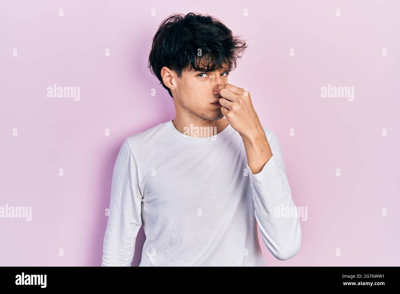 Handsome hipster young man wearing casual white shirt smelling ...