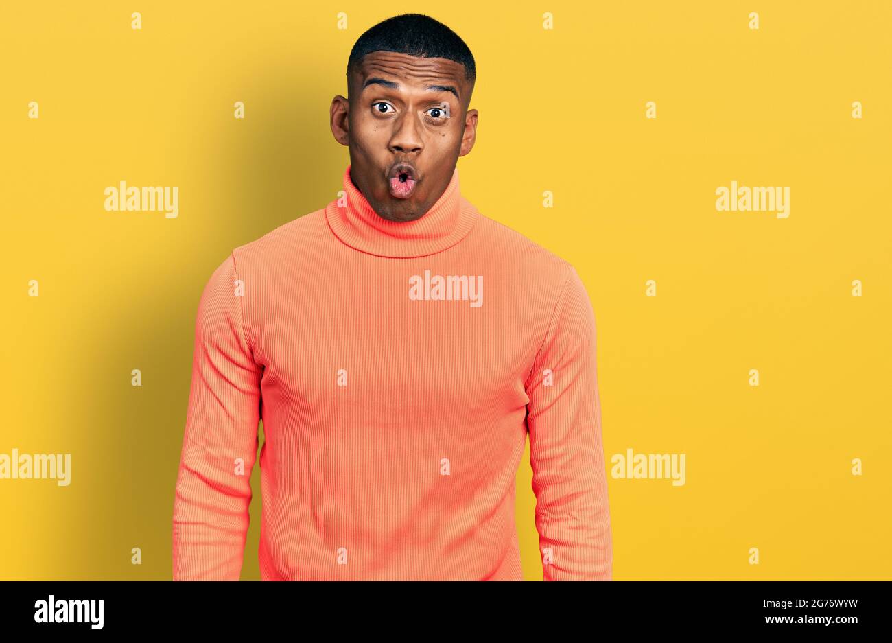 Young black man wearing orange turtleneck sweater scared and amazed ...