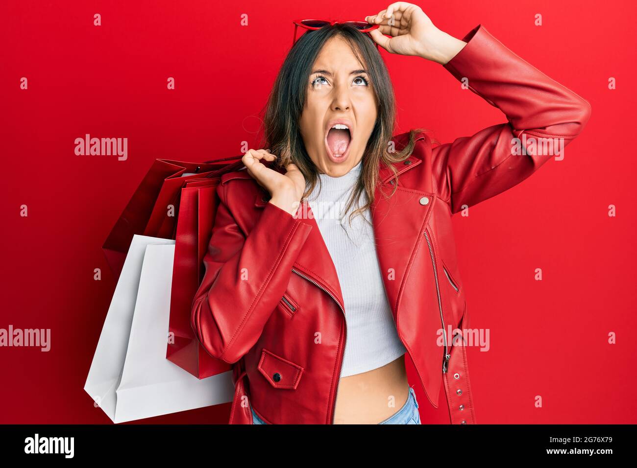 Young brunette woman holding shopping bags angry and mad screaming ...