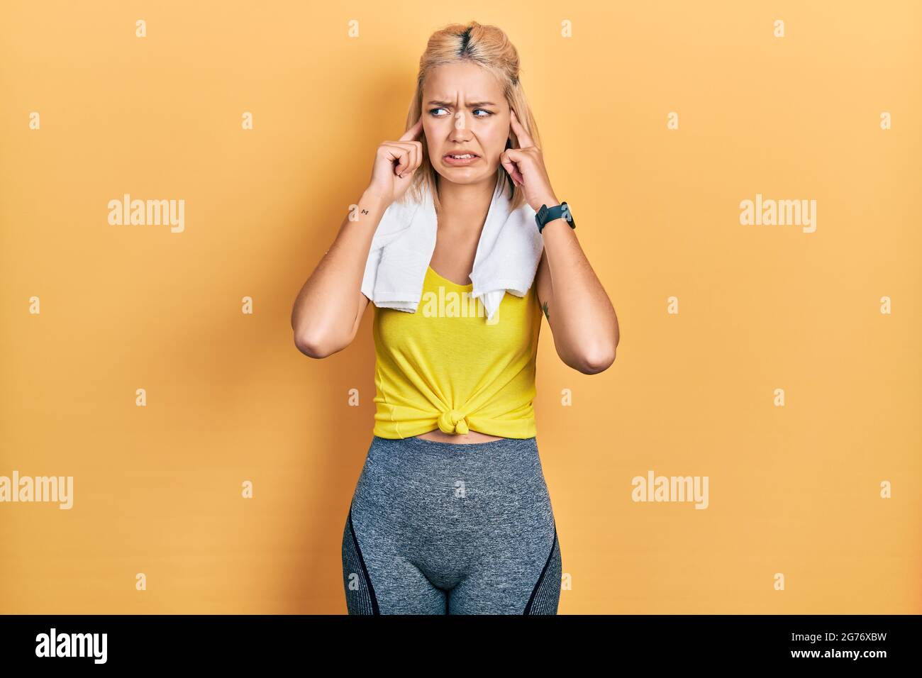 Beautiful blonde sports woman wearing workout outfit covering ears with ...
