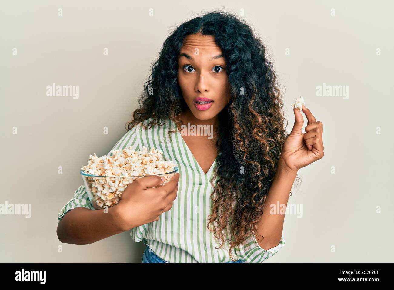 Young latin woman eating popcorn clueless and confused expression ...