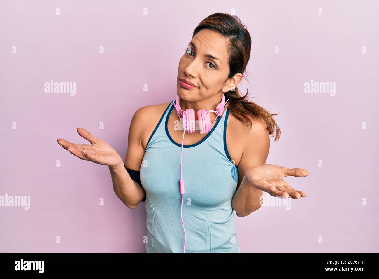 Young latin woman wearing gym clothes and using headphones clueless and ...