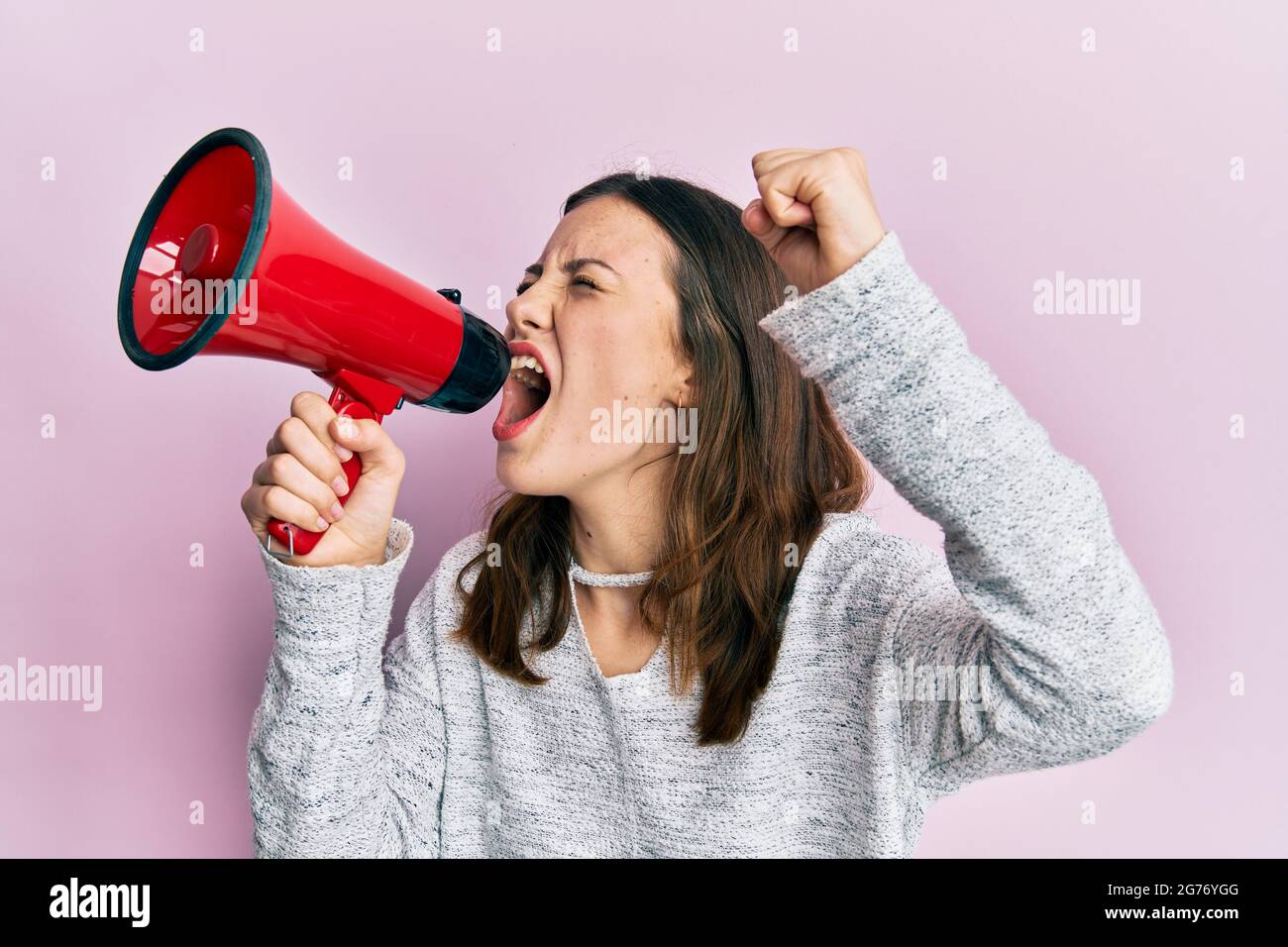 Young brunette woman shouting and screaming through megaphone over pink ...