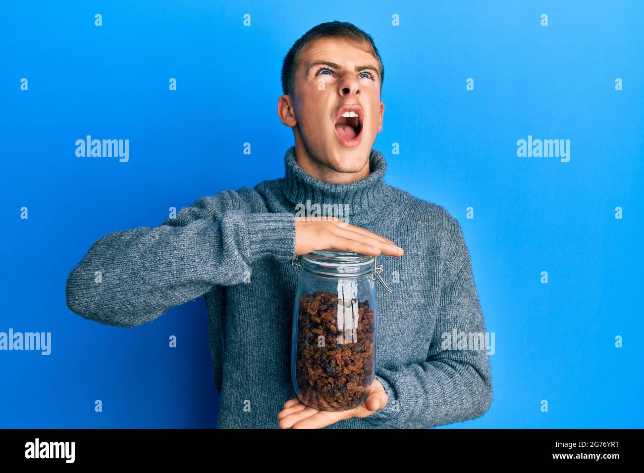 Young caucasian man holding jar of raisins angry and mad screaming ...