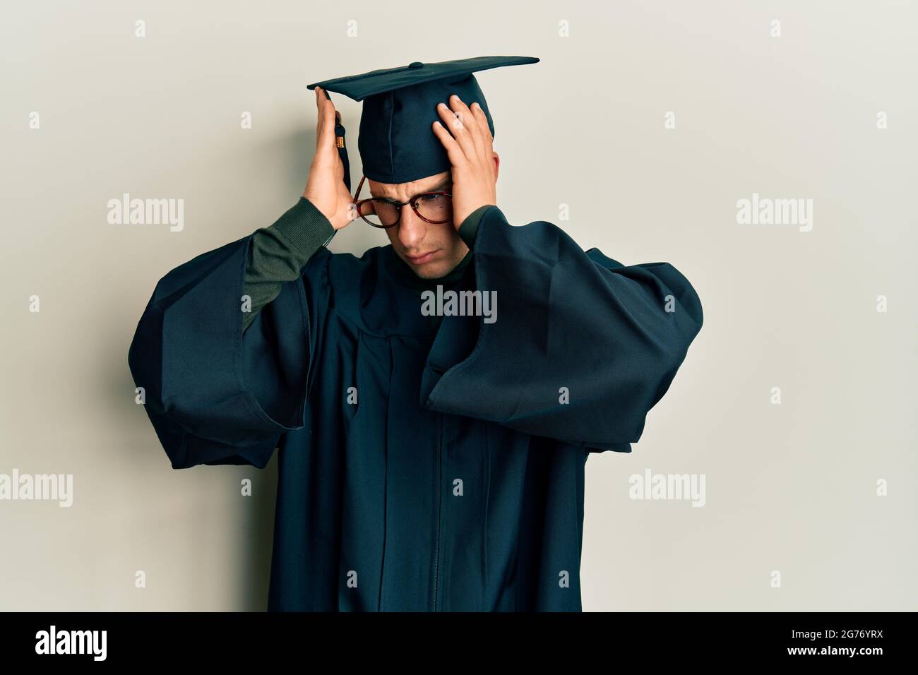 Young caucasian man wearing graduation cap and ceremony robe suffering ...