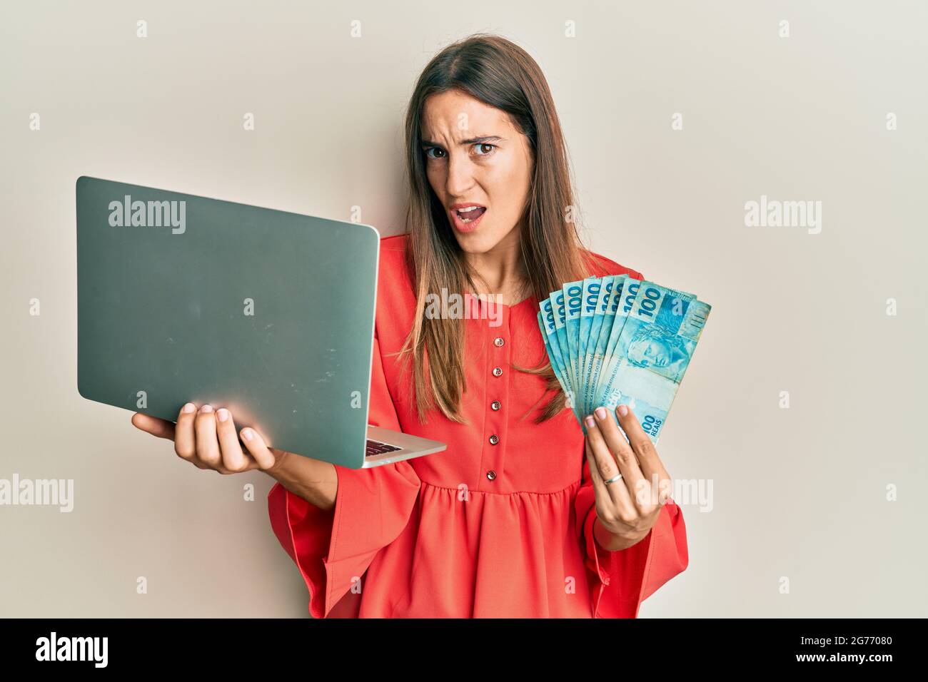 Young beautiful woman holding laptop and holding brazilian real ...