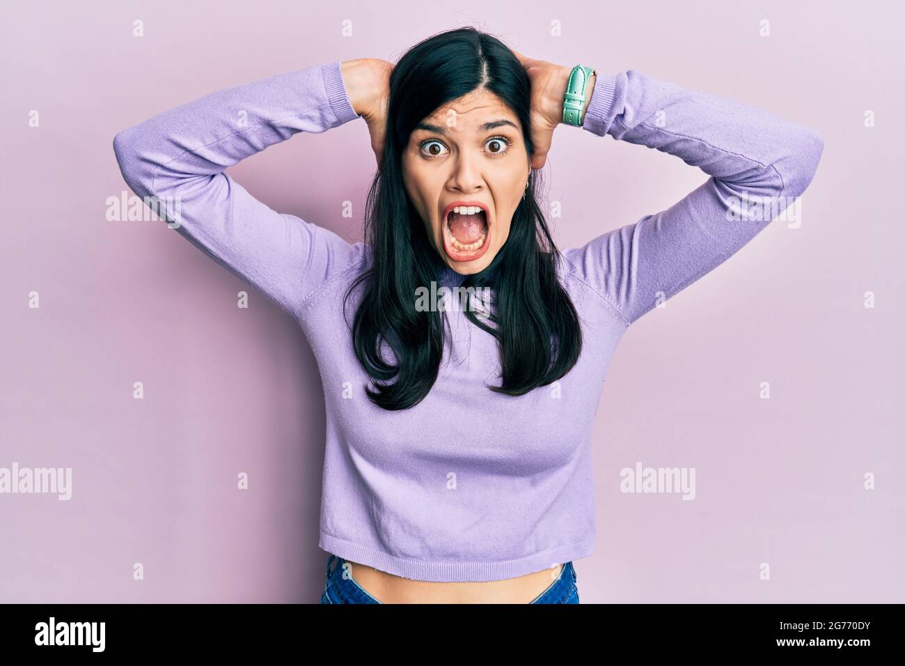 Young hispanic woman wearing casual clothes crazy and scared with hands ...