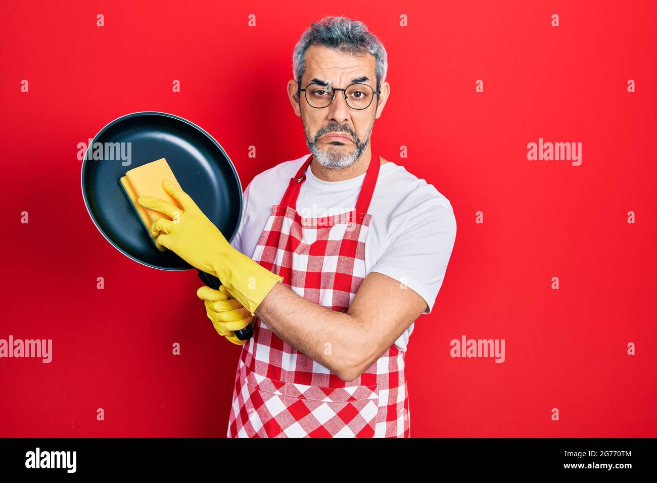 Handsome middle age man with grey hair wearing apron holding scourer ...