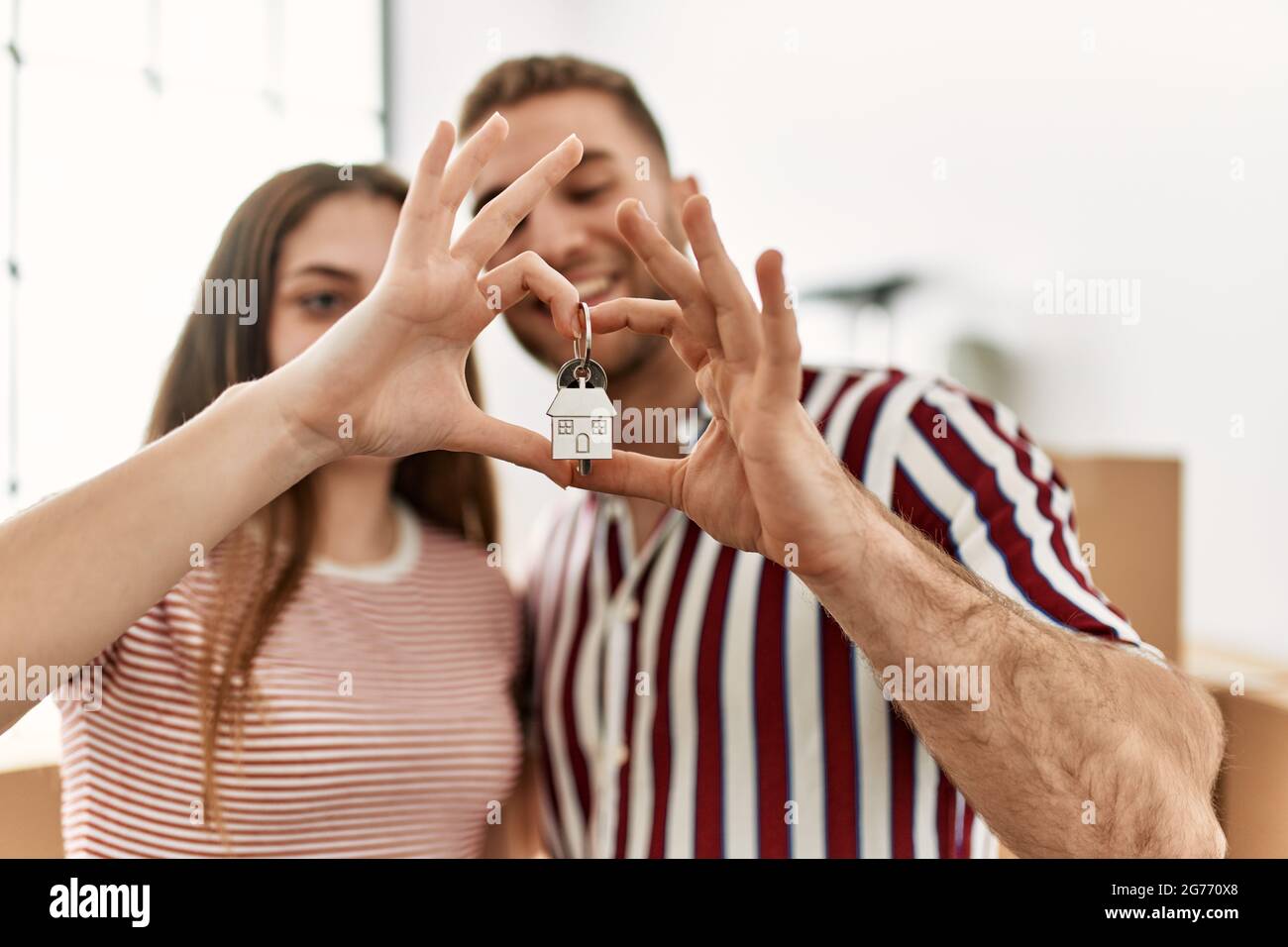 Young caucasian couple doing heart symbol with fingers and holding key ...