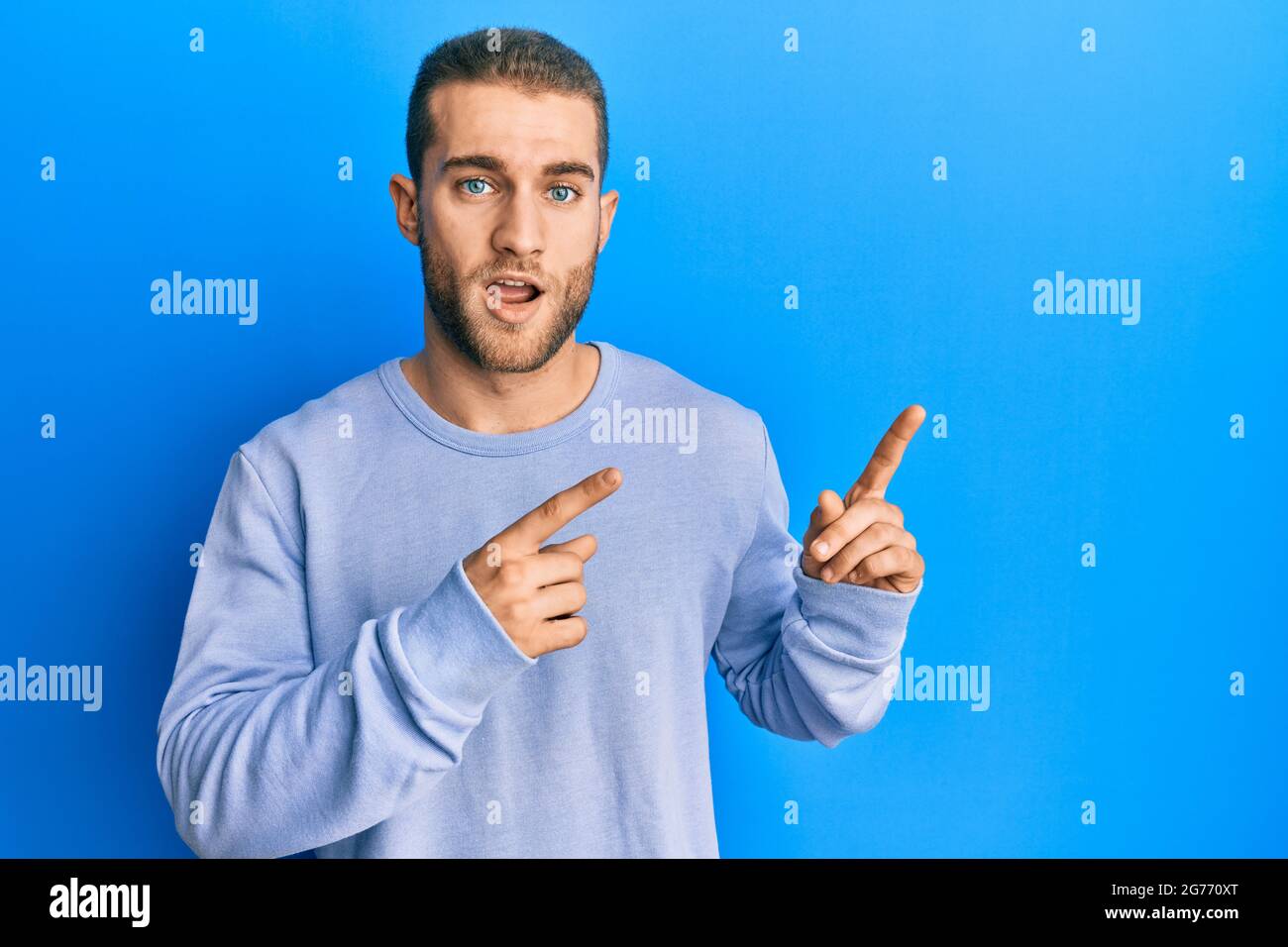 Young caucasian man pointing with fingers to the side in shock face ...
