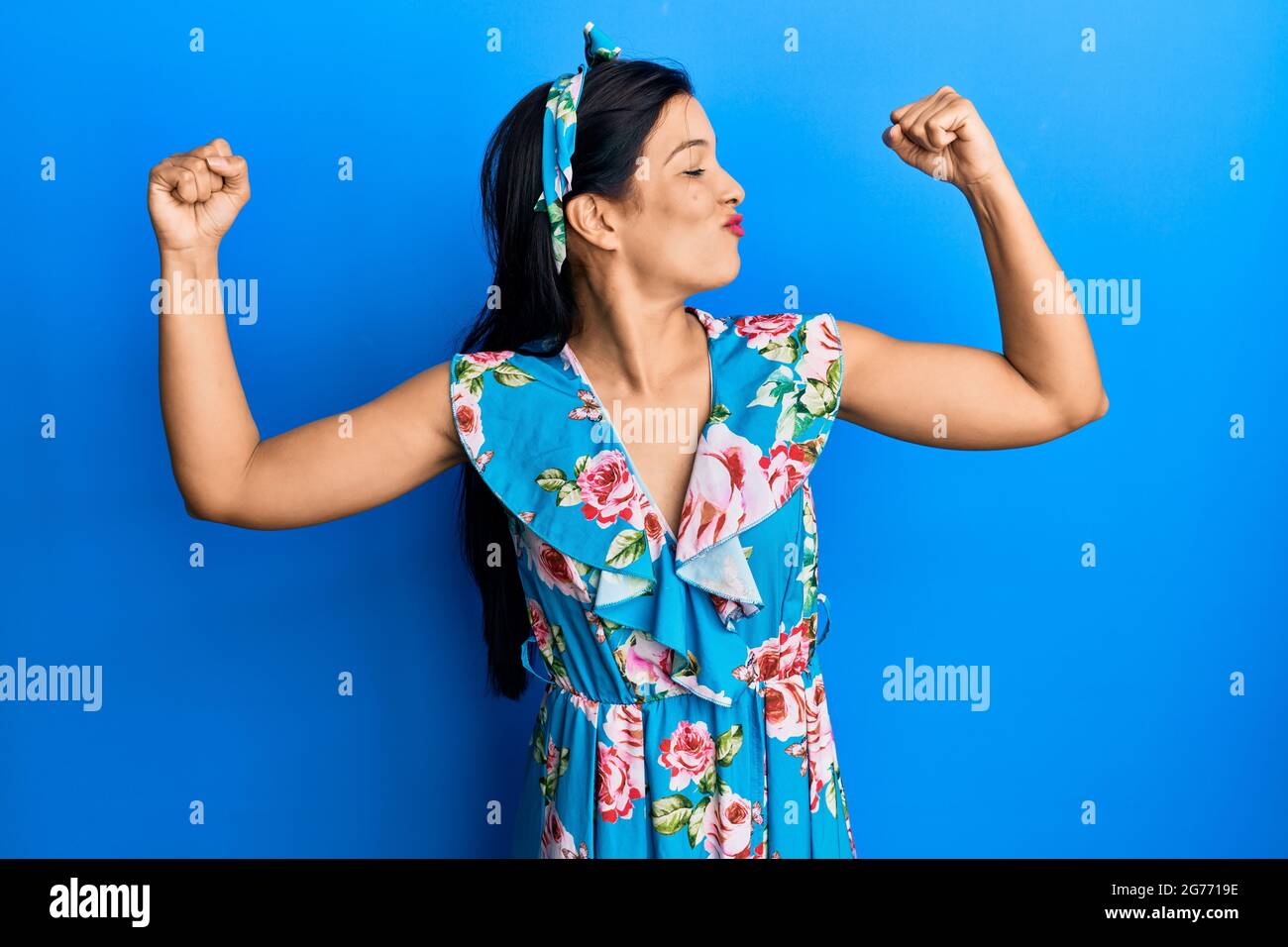 Young latin woman wearing casual clothes showing arms muscles smiling ...