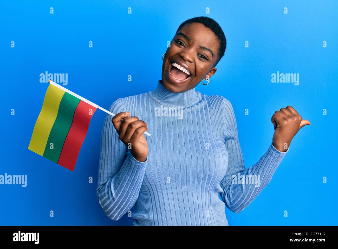 Young african american woman holding lithuania flag pointing thumb up ...