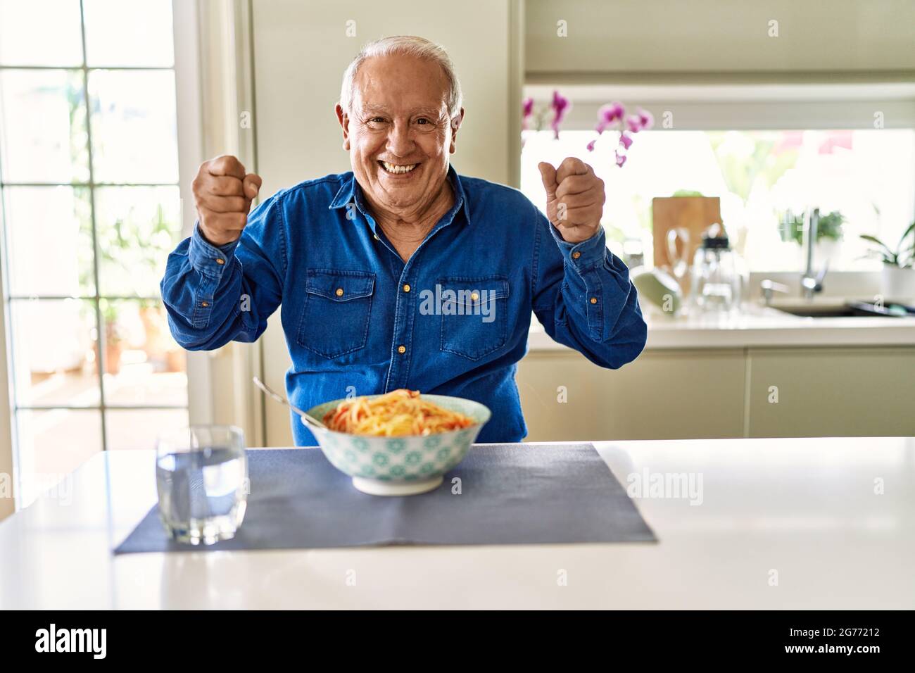Senior man with grey hair eating pasta spaghetti at home very happy and ...