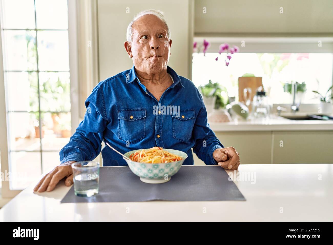 Senior man with grey hair eating pasta spaghetti at home making fish ...