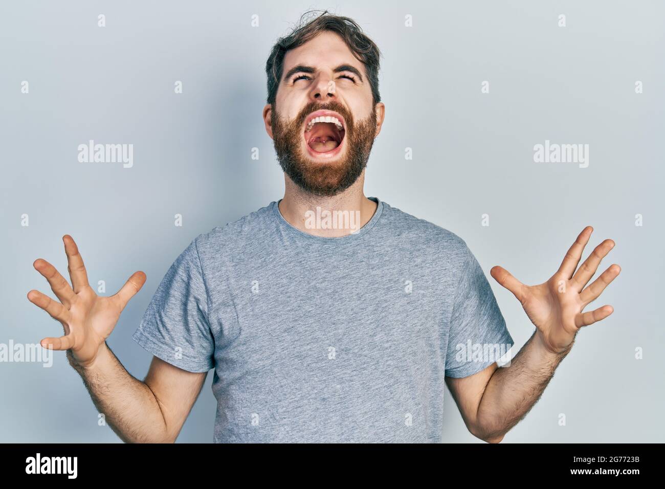 Caucasian man with beard wearing casual grey t shirt crazy and mad ...