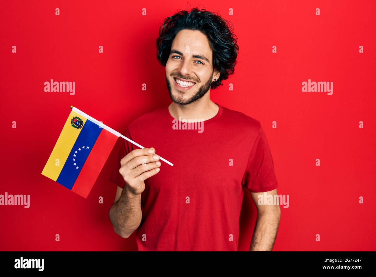 Handsome hispanic man holding venezuelan flag looking positive and ...