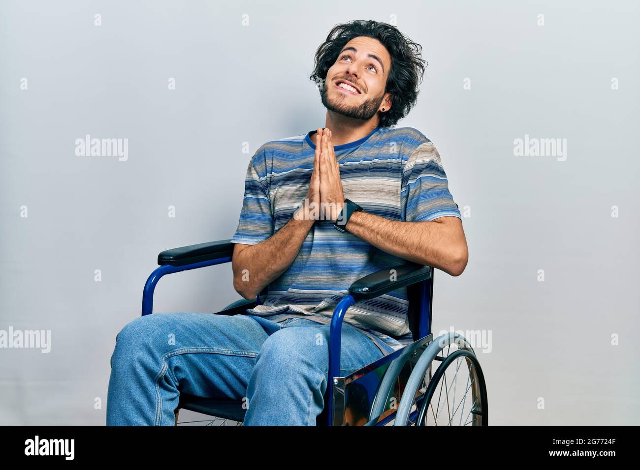 Handsome hispanic man sitting on wheelchair begging and praying with ...
