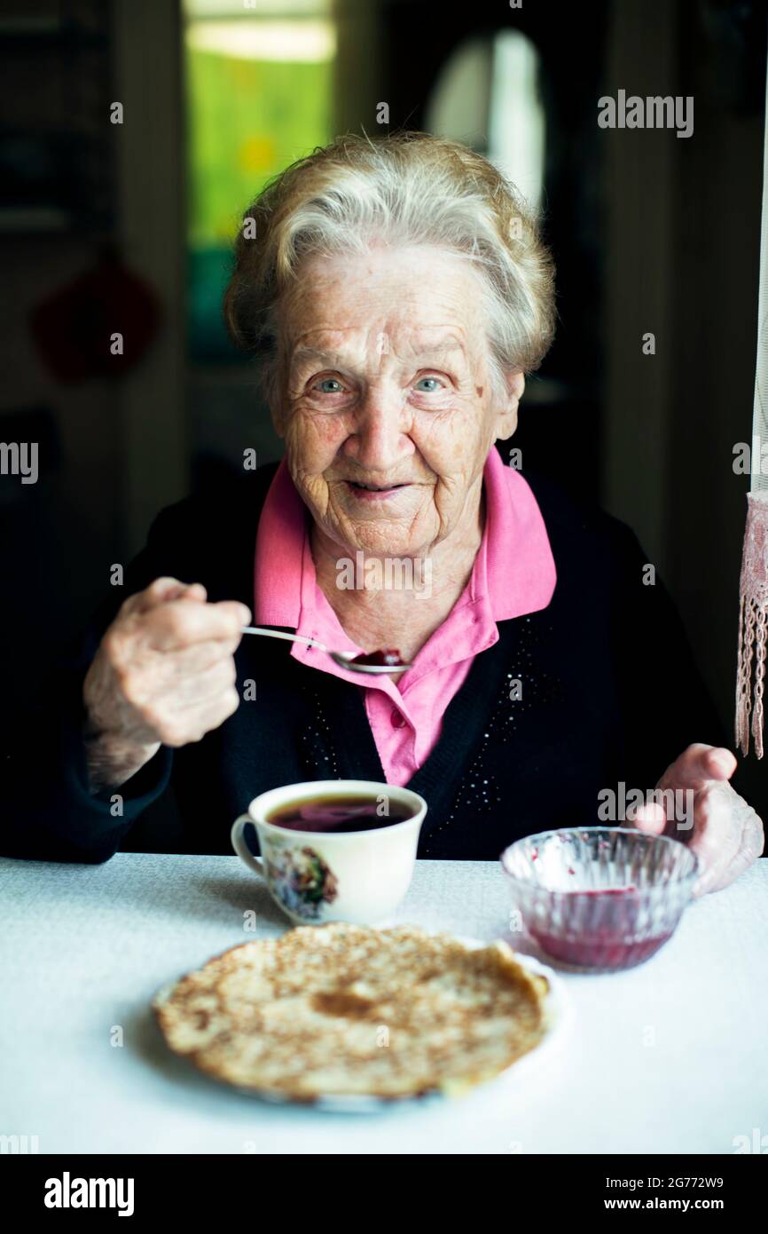 An old woman pensioner drinks tea with pastries at her home Stock Photo ...