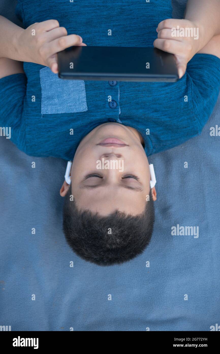 A vertical shot of a young boy laying down on the ground outdoors ...
