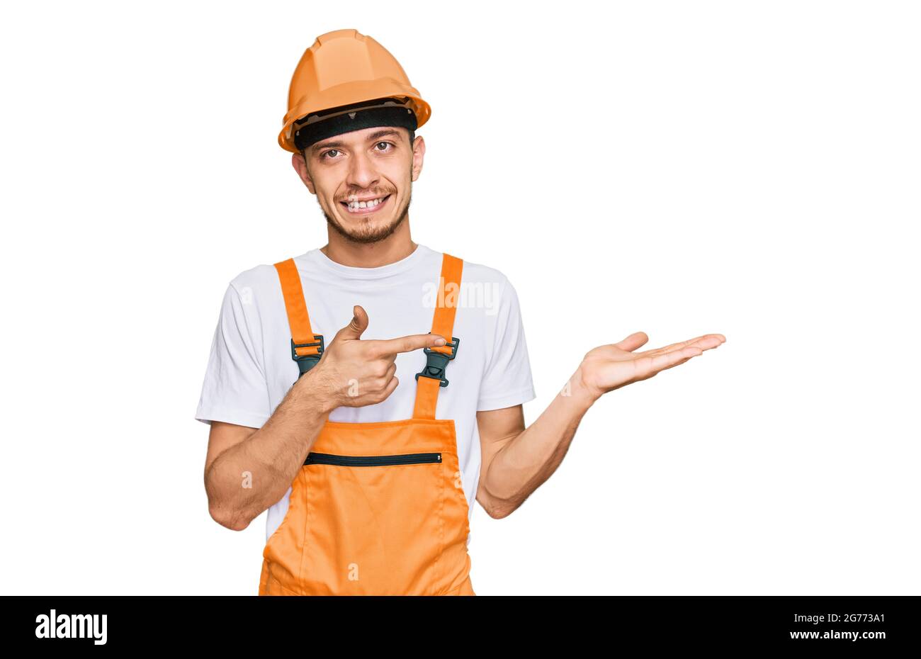 Hispanic young man wearing handyman uniform and safety hardhat amazed ...