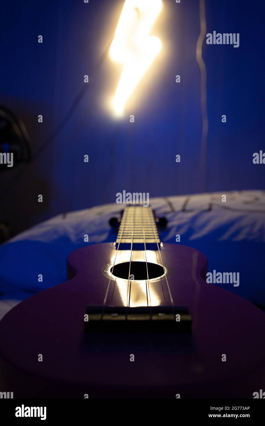 A vertical shot of a ukulele on a bed under the lights with a blurry ...
