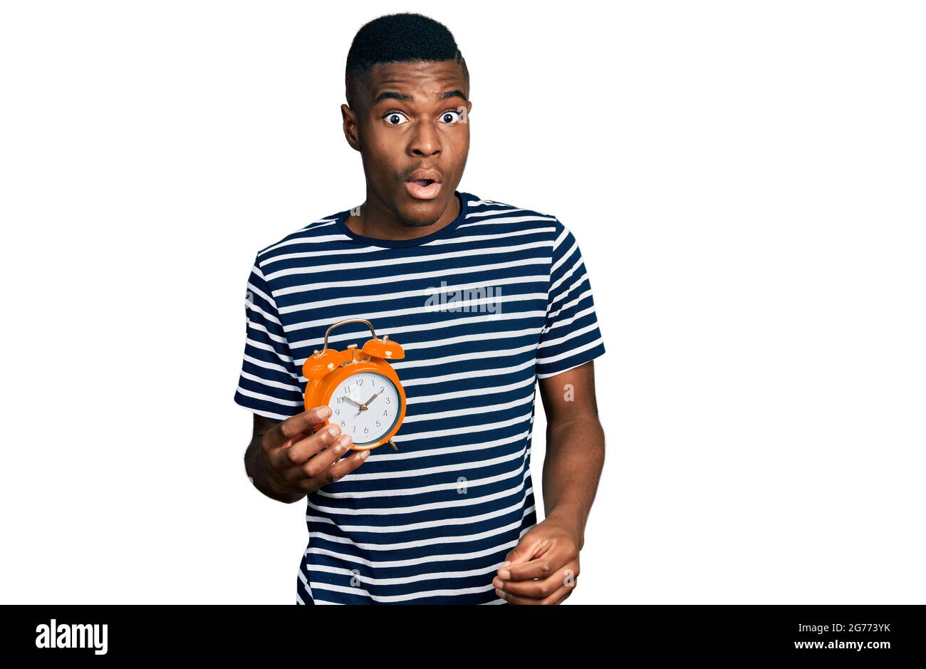 Young african american man holding alarm clock scared and amazed with ...