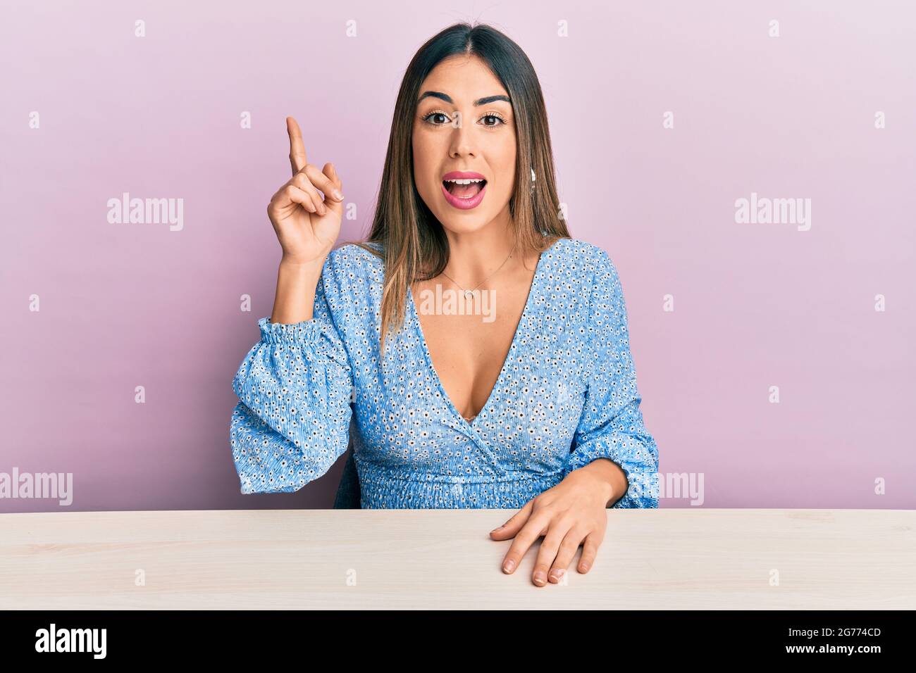 Young hispanic woman wearing casual clothes sitting on the table ...