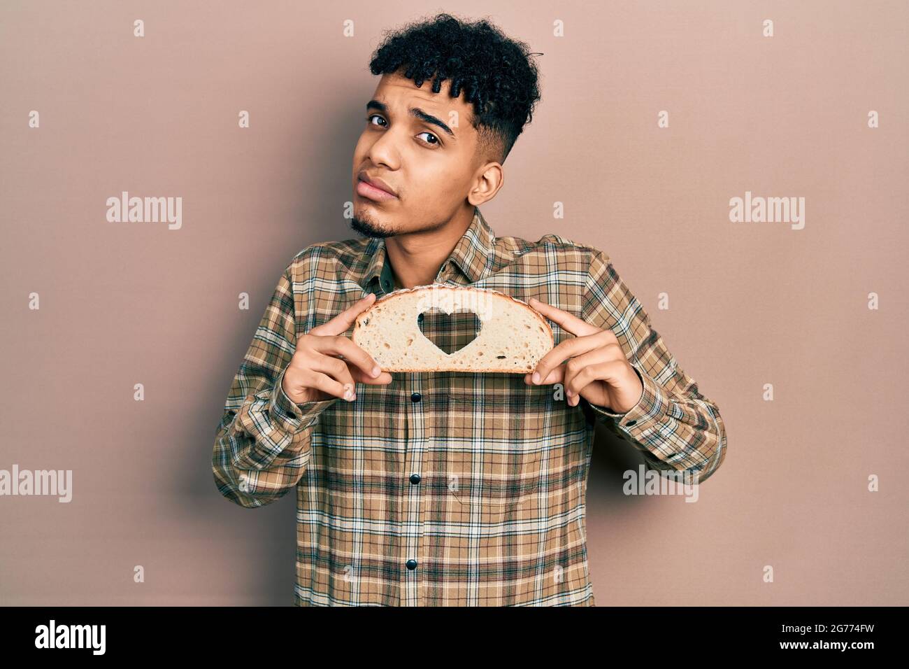 Young african american man holding bread loaf with heart shape clueless ...