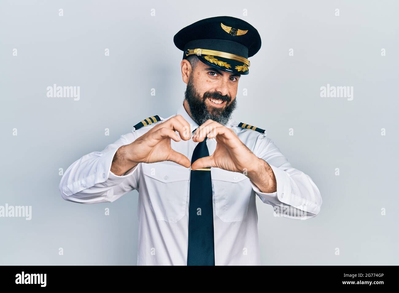 Young hispanic man wearing airplane pilot uniform smiling in love doing ...