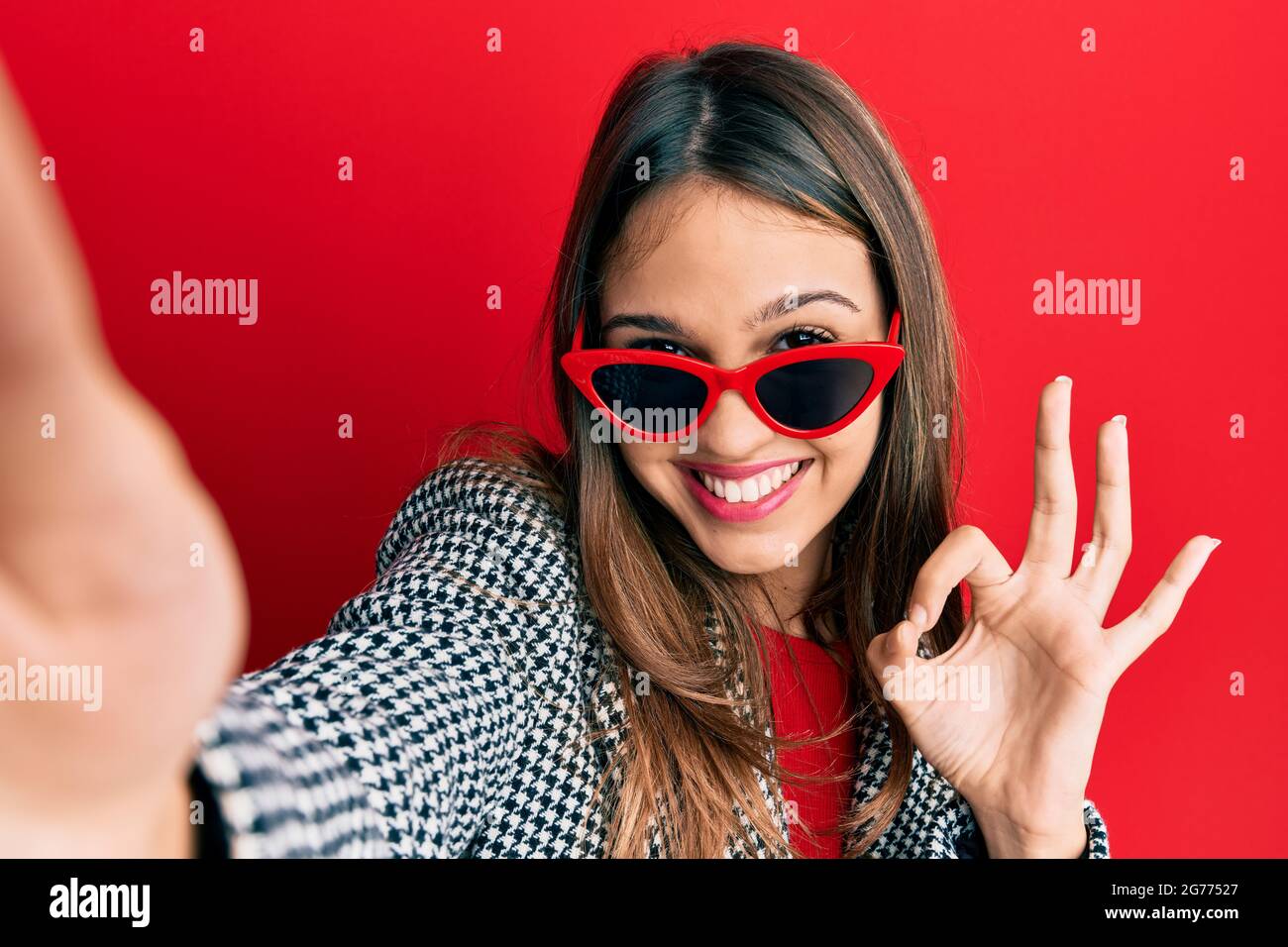 Young brunette woman taking a selfie photo wearing sunglasses doing ok ...