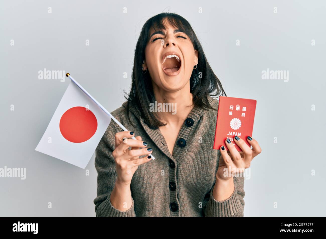 Young hispanic woman holding japan flag and passport angry and mad ...