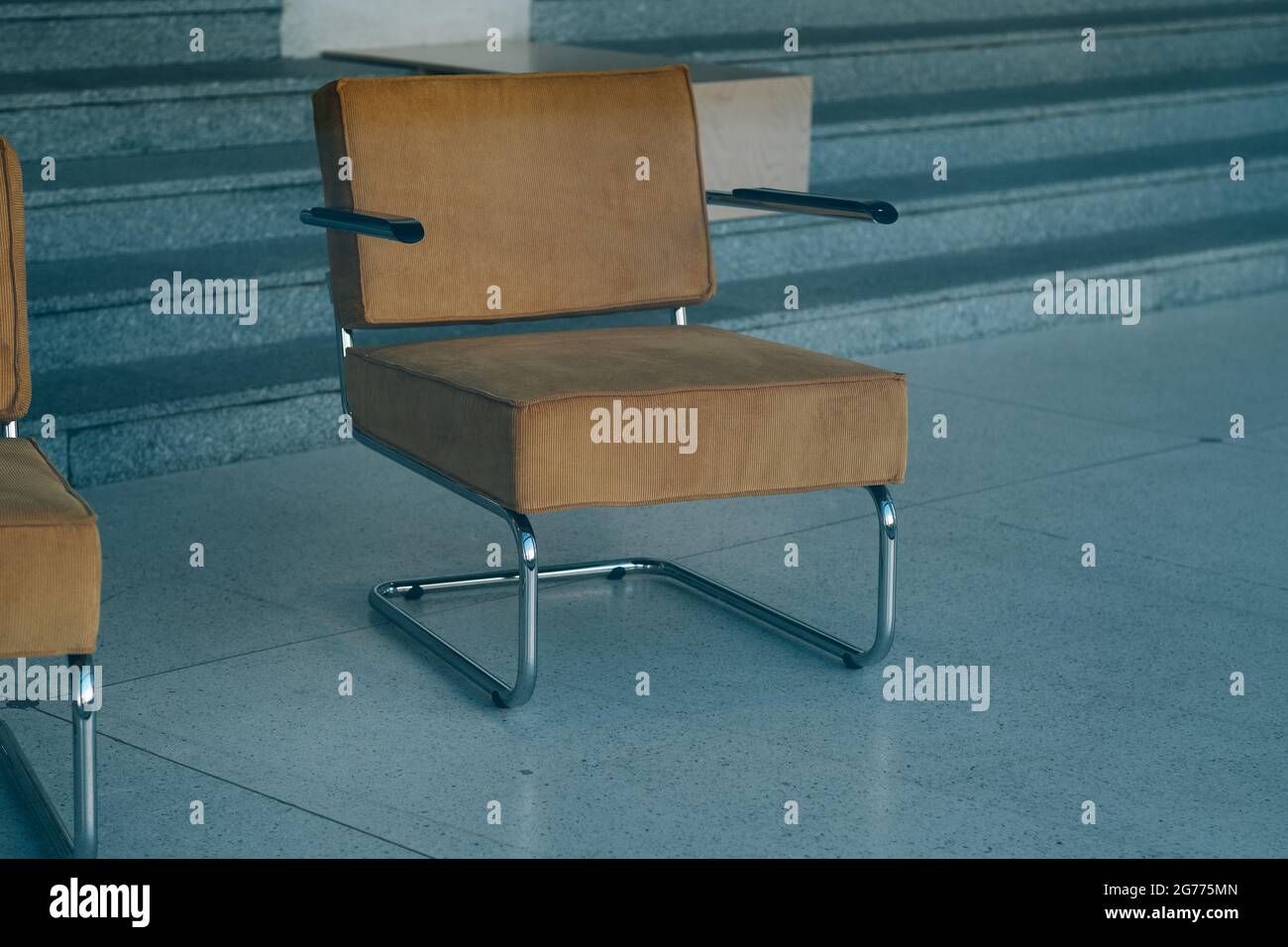 A brown cushioned chair with metal legs on a smooth tile floor in front ...