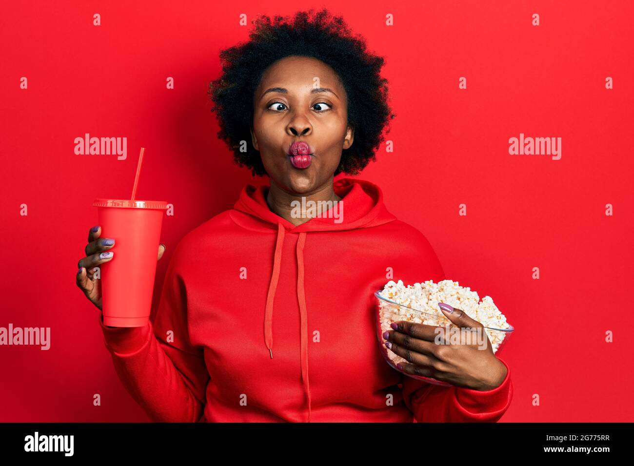 Young african american woman eating popcorn and drinking soda making ...