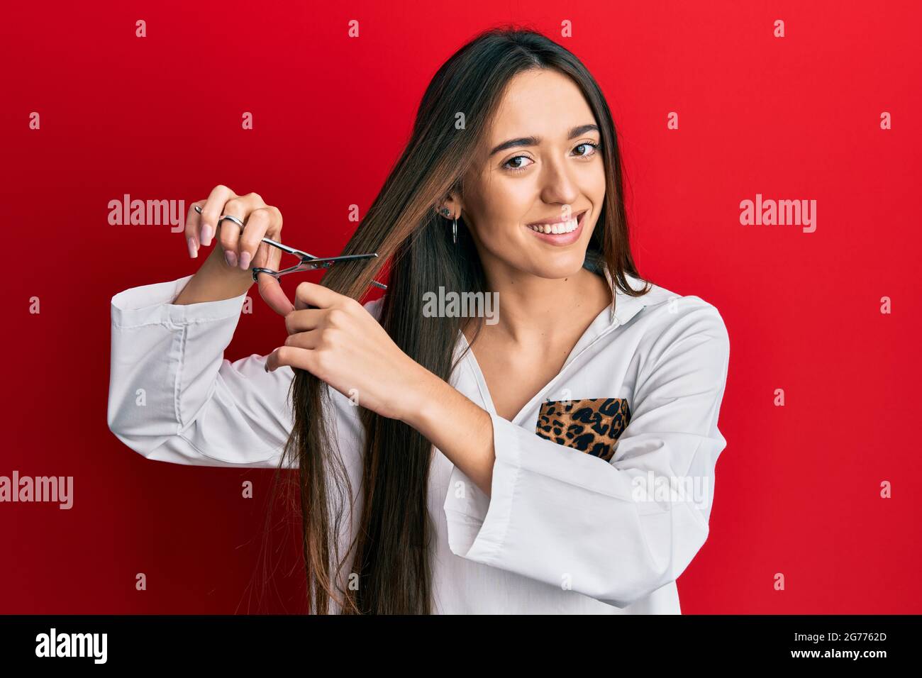 Young hispanic girl cutting hair using scissors smiling with a happy ...
