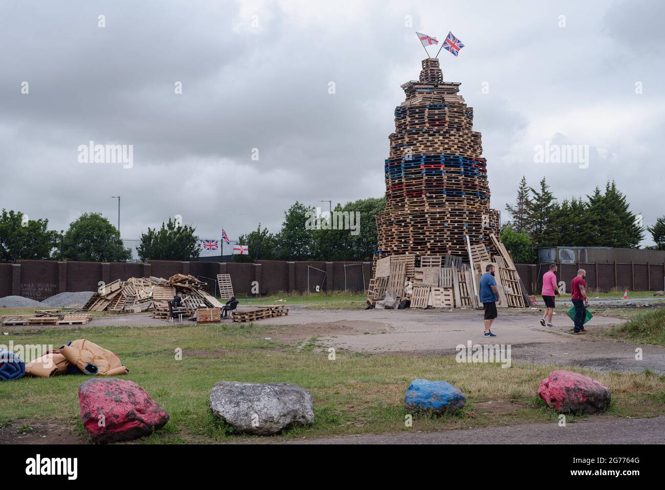 Three men walk past a bonfire with a Union Jack and Ulster flags ...