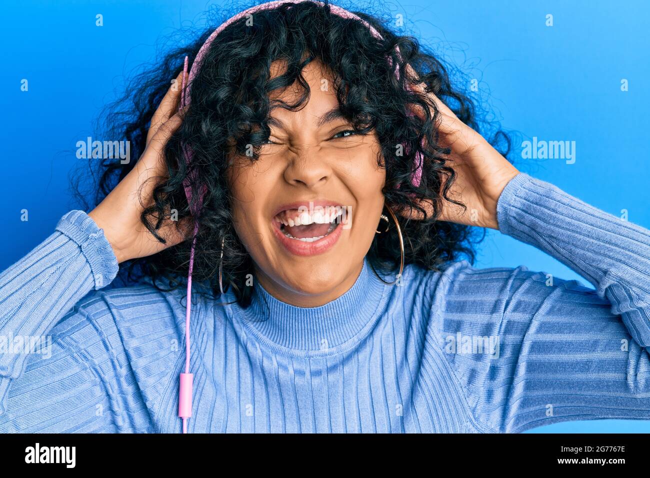 Young hispanic woman listening to music using headphones smiling and ...