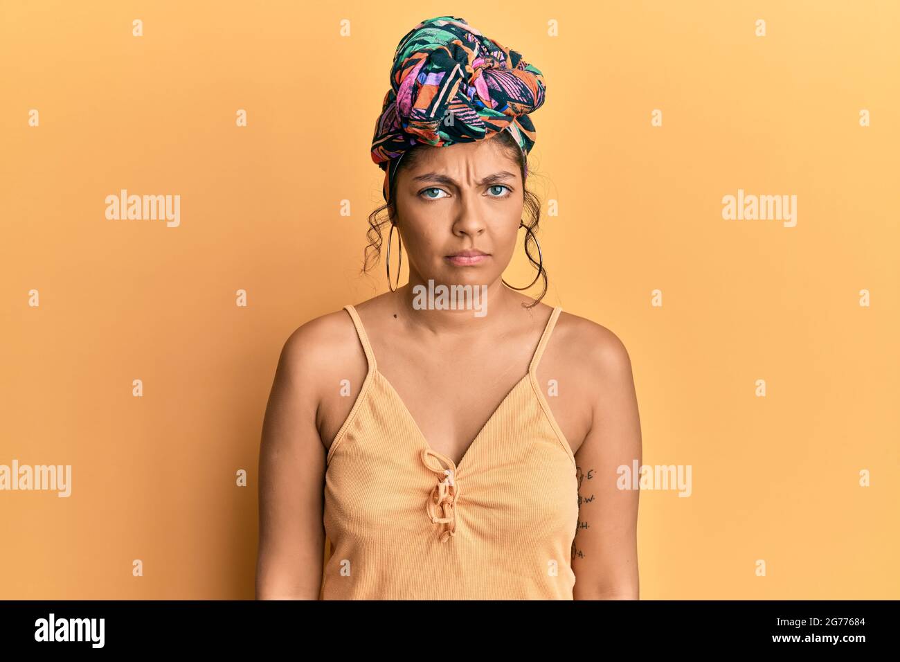 Young hispanic girl wearing hair turban over yellow background skeptic ...