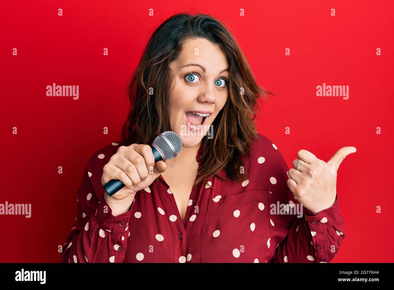 Young caucasian woman singing song using microphone pointing thumb up ...
