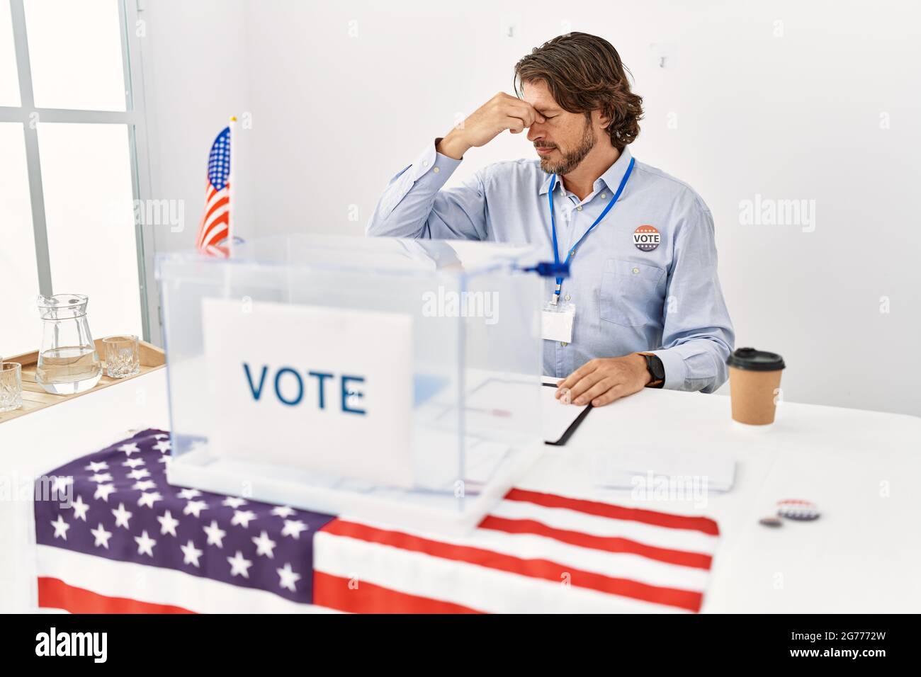 Handsome middle age man sitting at voting stand tired rubbing nose and ...