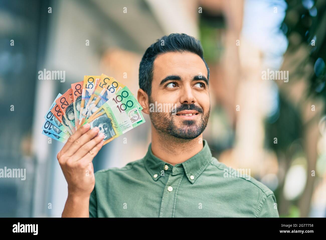 Young hispanic man smiling happy holding australian dollars at the city ...