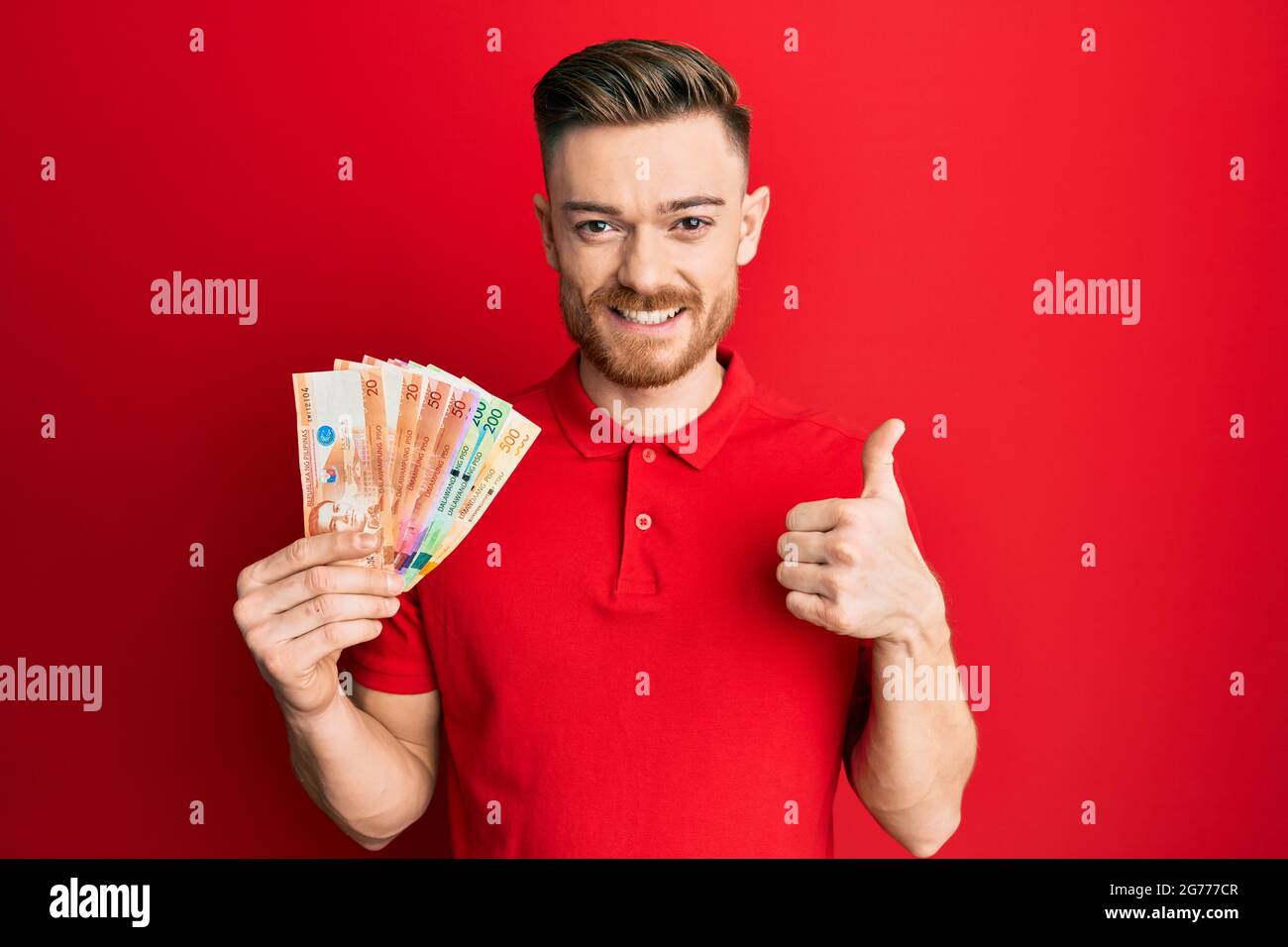 Young redhead man holding philippine peso banknotes smiling happy and ...