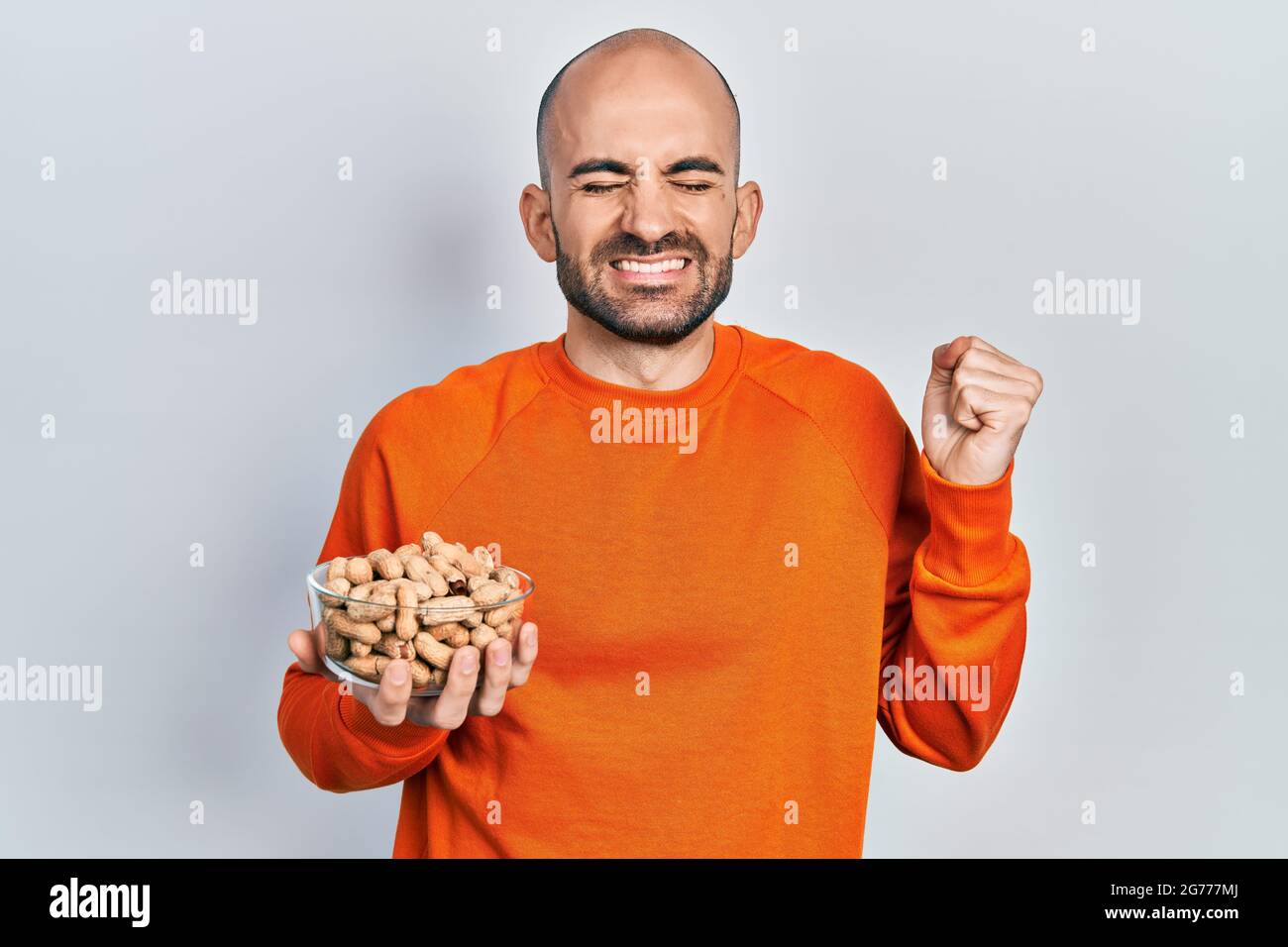 Young bald man holding peanuts screaming proud, celebrating victory and ...